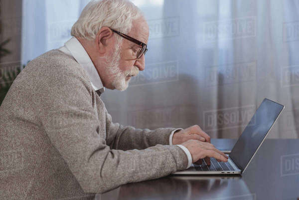 Side view of handsome grey hair man using laptop at home - Royalty-free ...