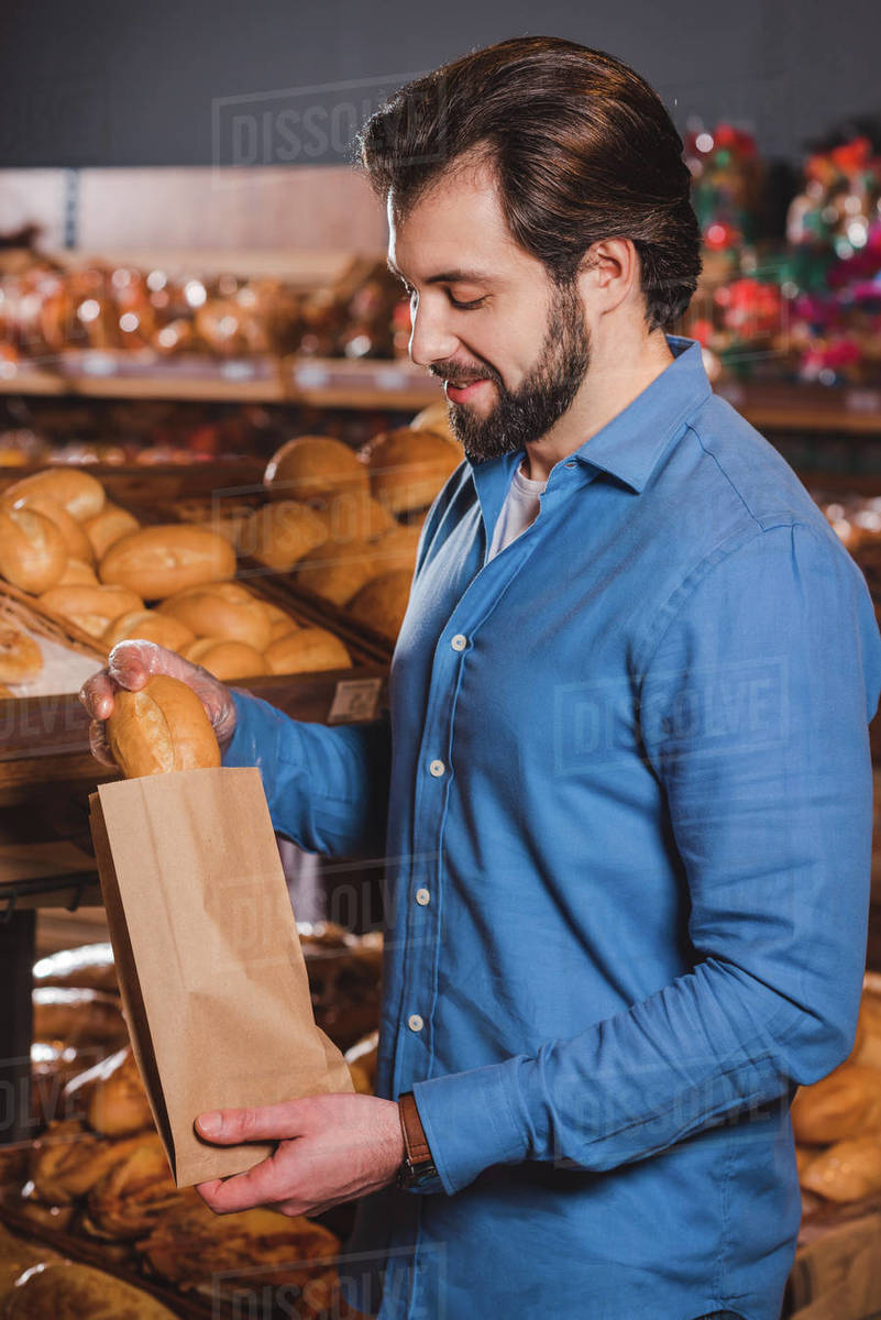 Side view of smiling man choosing bread in hypermarket - Royalty-free ...