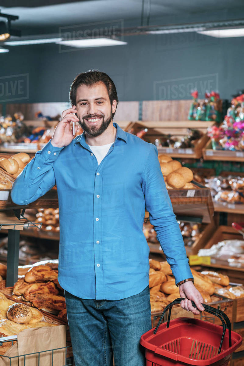Portrait of smiling shopper talking on smartphone in grocery shop ...
