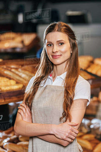 Portrait of smiling shop assistant in apron looking at camera in ...