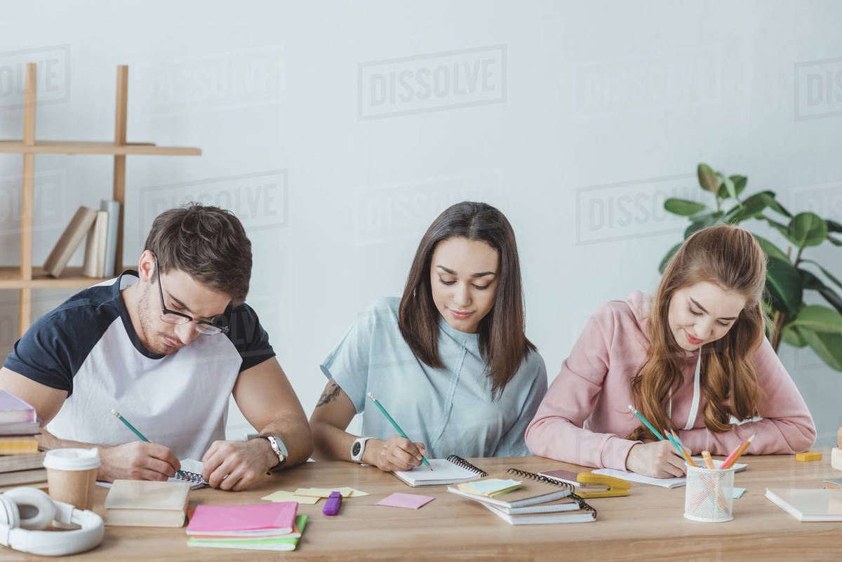 Young multicultural students writing in copybooks at table - Royalty ...