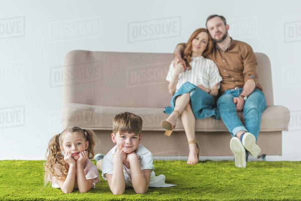 Happy parents sitting on couch and looking at beautiful children lying ...