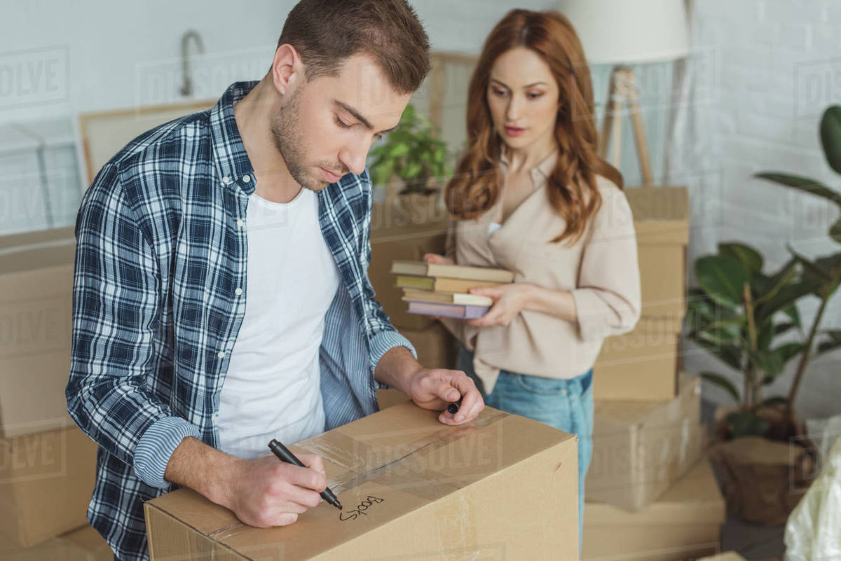 Man signing cardboard box with wife with books in hands near by, moving ...