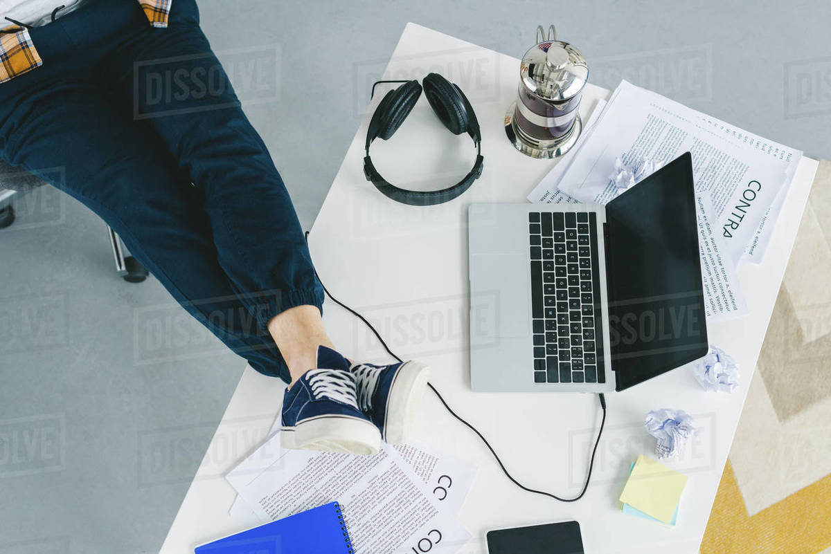 Close-up view of male feet on table with laptop in light office ...