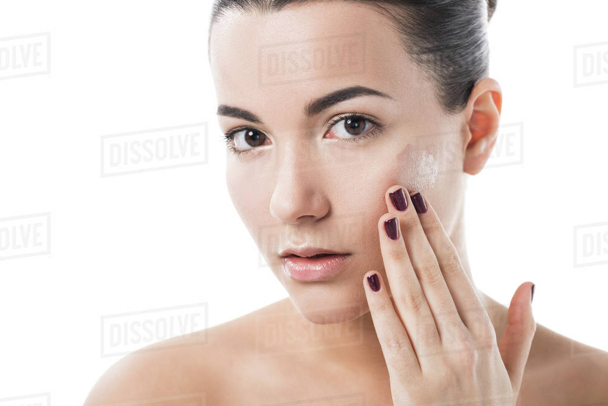 Beautiful girl applying foundation cream on cheek and looking at camera ...