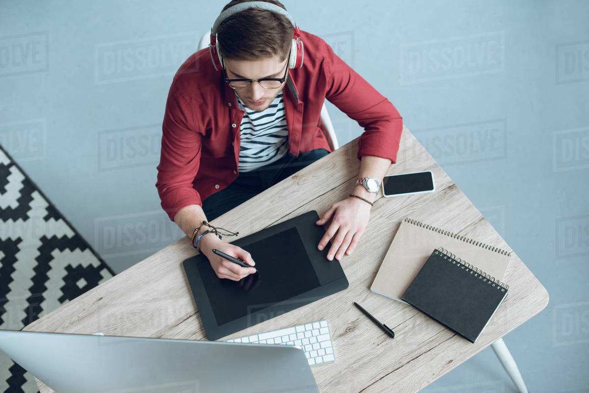 Young man in headphones using graphic tablet by table with computer ...