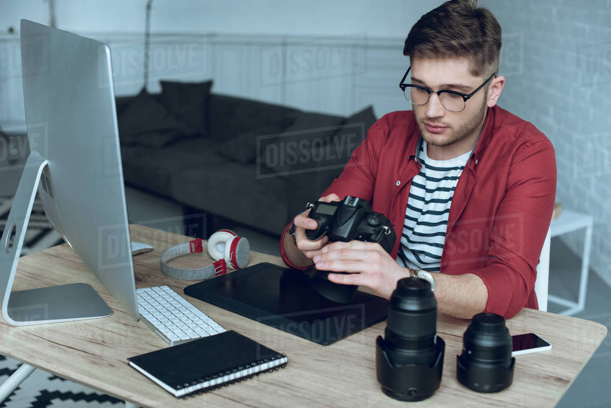 Man freelancer with camera in hands at work by table with computer and ...