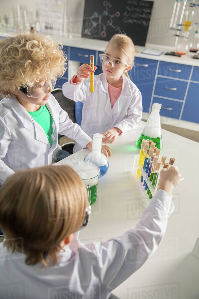 Schoolchildren in lab coats making experiment with test tubes in ...