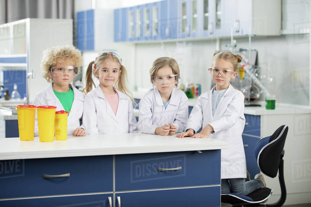 Four kids in science laboratory wearing coats and standing at table ...