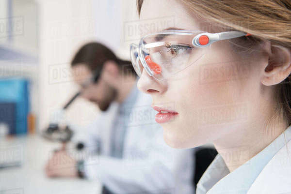 Side view of attractive female scientist in protective glasses ...