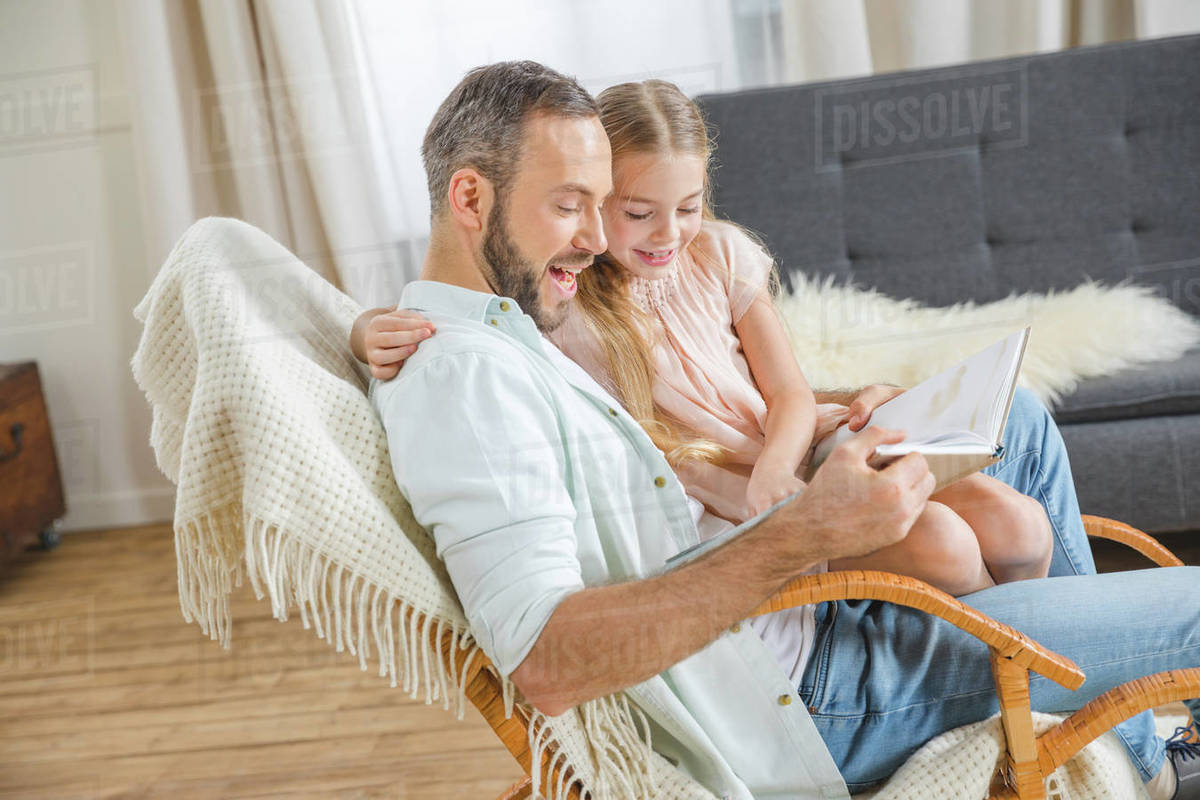 Happy father and daughter sitting in rocking chair and reading book ...