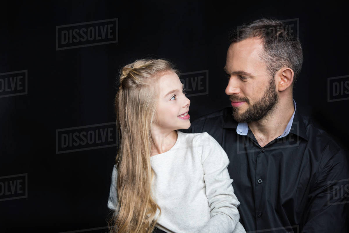 Smiling father and daughter looking at each other isolated on black ...