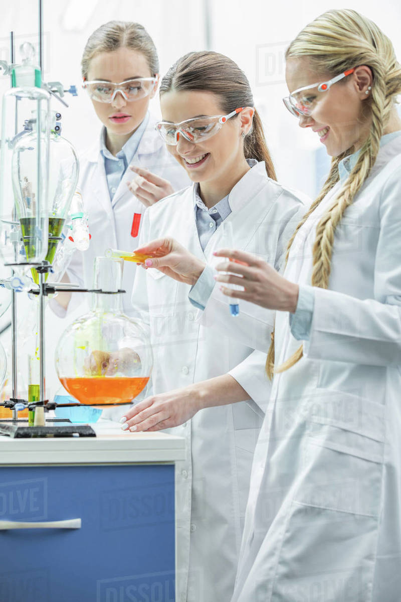 Three young smiling female scientists making experiment in chemical lab ...