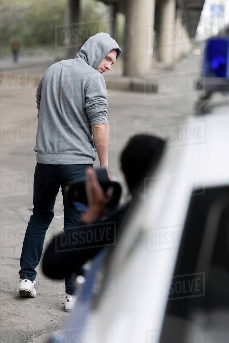 Policeman looking on hooded young man walking away on street out of ...