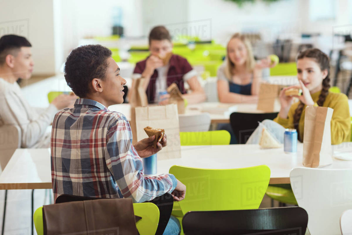 Group of high school students chatting while taking lunch at school ...