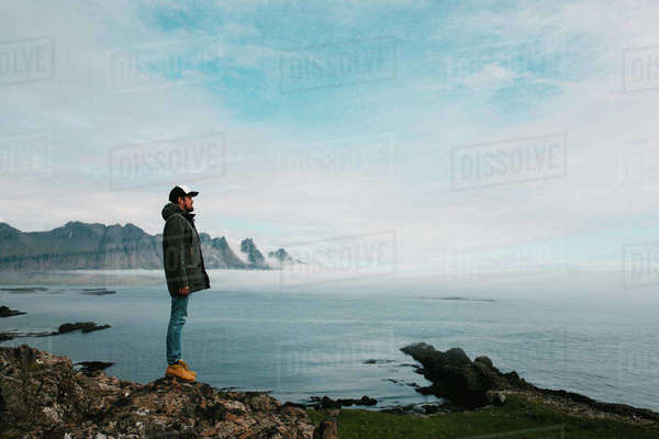 Side view of young man standing on rock and looking at beautiful ...