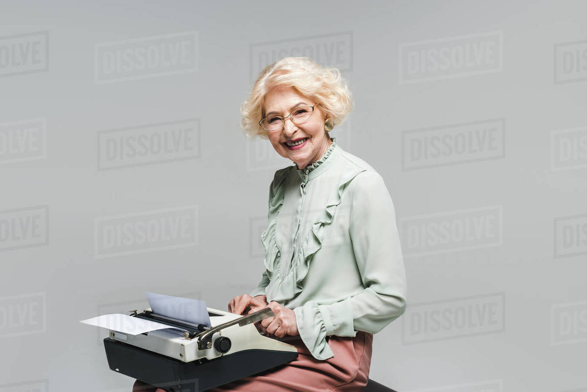 Happy senior woman using typewriter on grey - Royalty-free Stock Photo ...