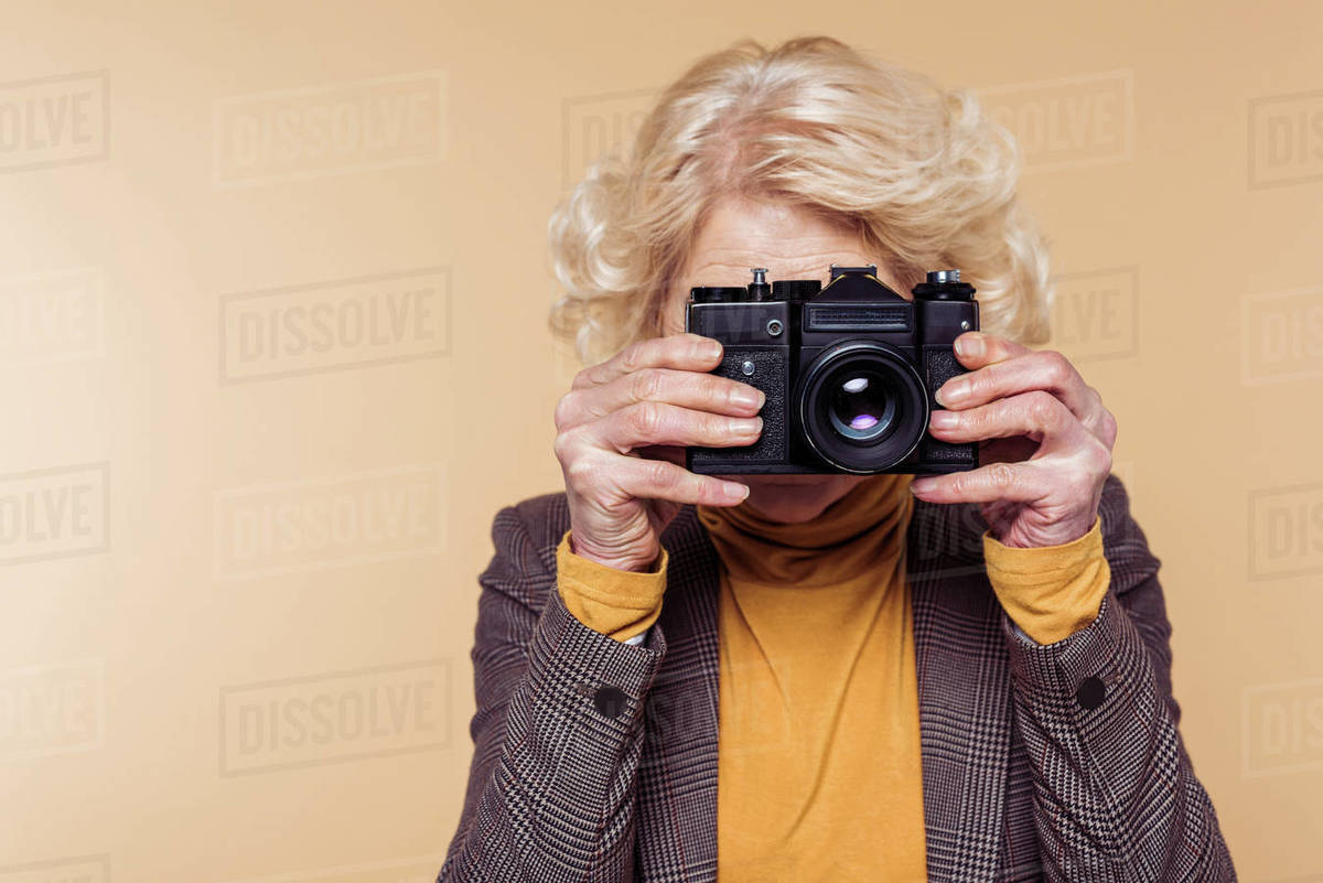 Senior woman shooting on film camera isolated on beige background ...