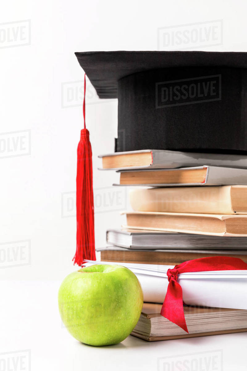Apple near diploma and pile of books with academic cap on top isolated ...