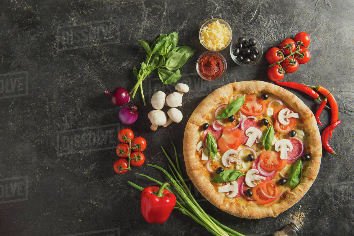 Flat lay with Italian pizza and fresh ingredients on dark surface ...