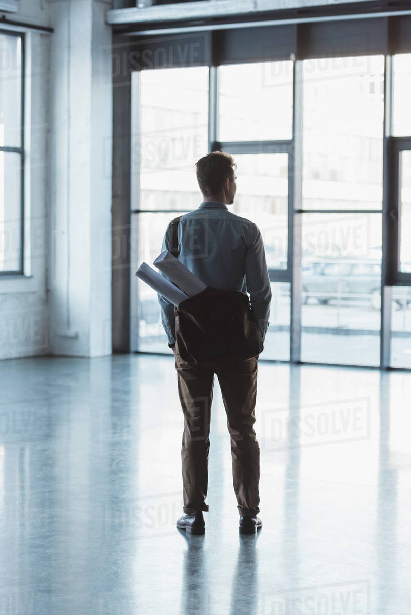 Back view of architect with bag full of blueprints standing in empty ...