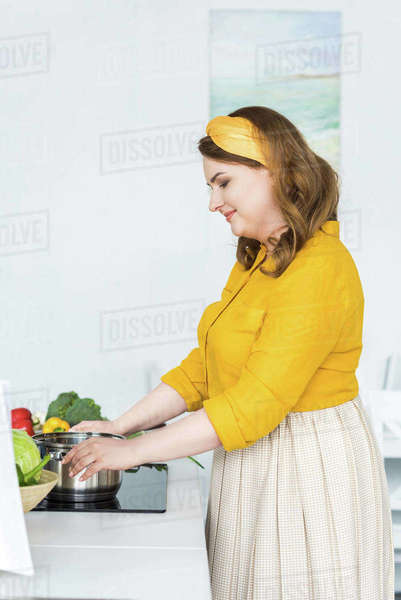 Side view of beautiful woman cooking at electric stove in kitchen ...