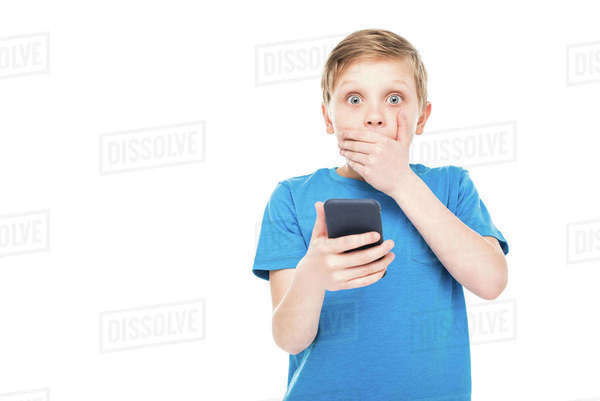 Shocked little boy holding smartphone and looking at camera isolated on ...