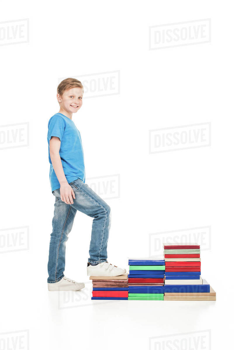 Cute little boy stepping on books and smiling at camera isolated on ...