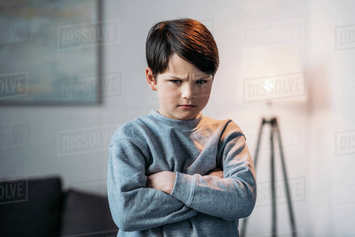 Portrait of offended boy with crossed arms looking at camera at home ...