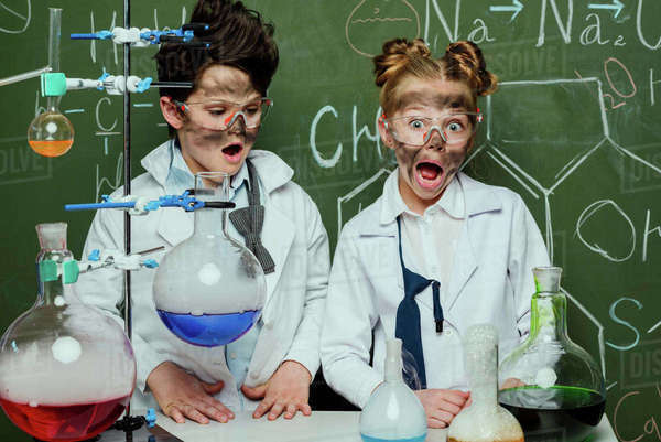 Little kids in white coats with chalkboard behind in science laboratory ...