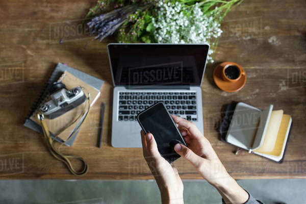 Person using smartphone and laptop at workspace with notebooks and ...