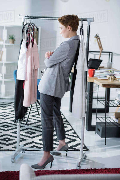 Serious fashion designer standing under rack with clothing - Royalty ...