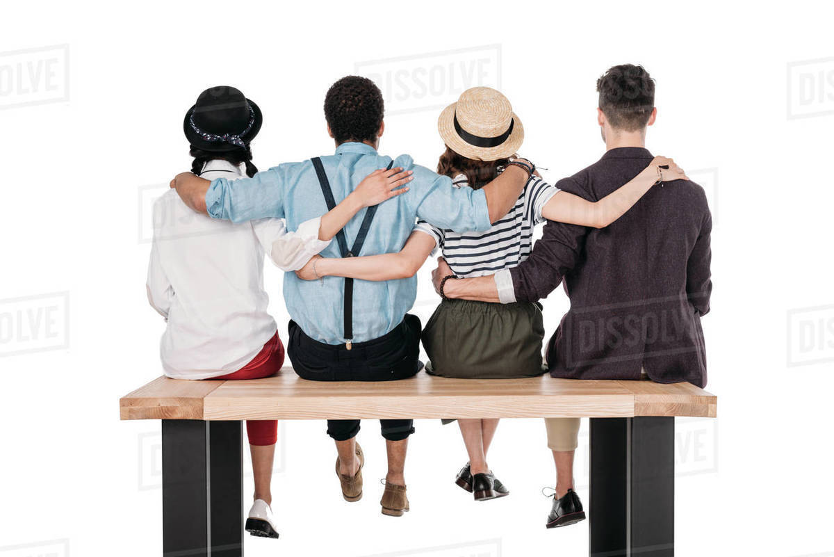 Back view of stylish young friends sitting embracing on bench isolated ...