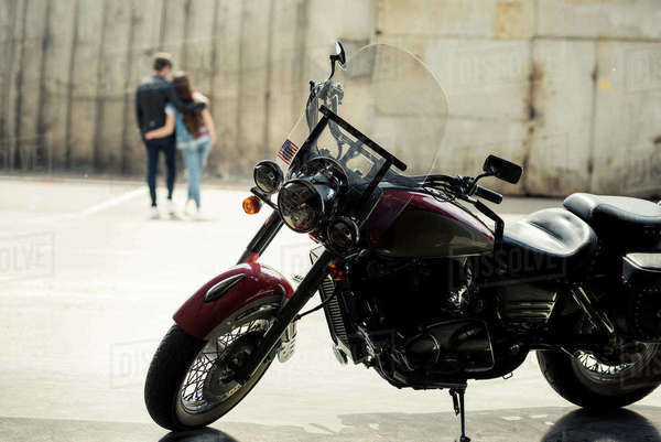 Close-up view of motorcycle standing on pavement and young couple ...