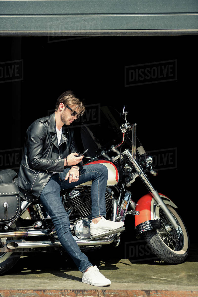 Handsome young man in sunglasses and leather jacket sitting on ...