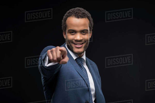 Portrait of smiling businessman pointing at camera isolated on black ...