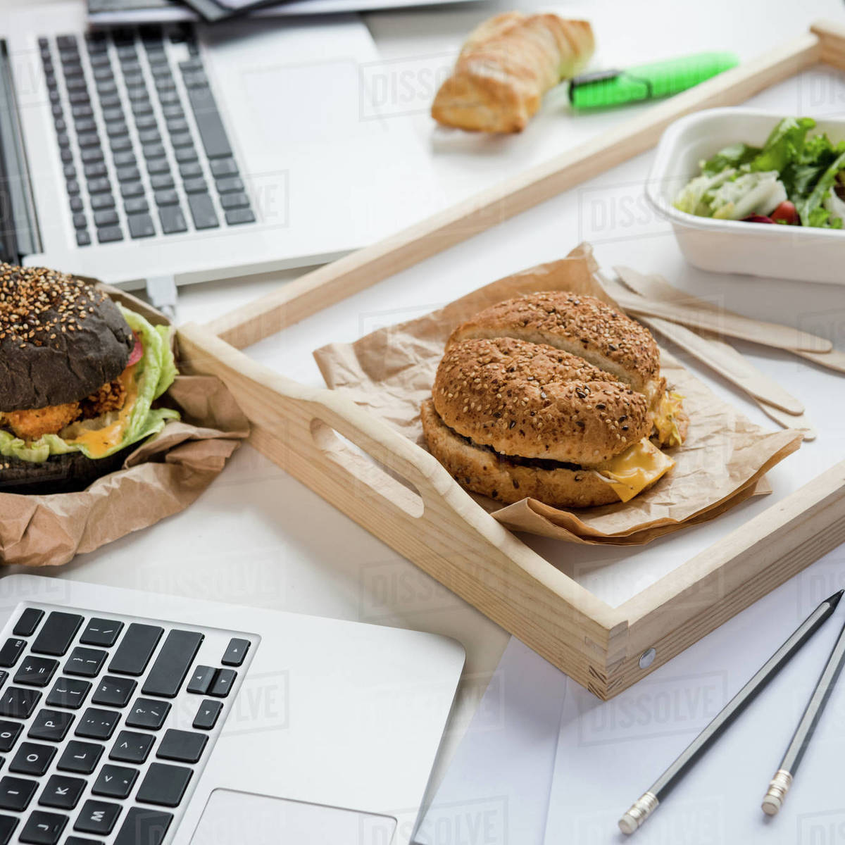 Close up of tasty burgers with fresh salad and bread loaf with laptops ...