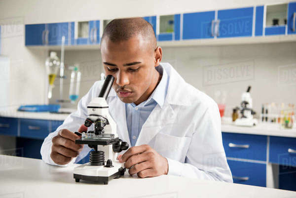Young technician in uniform using a microscope in laboratory ...