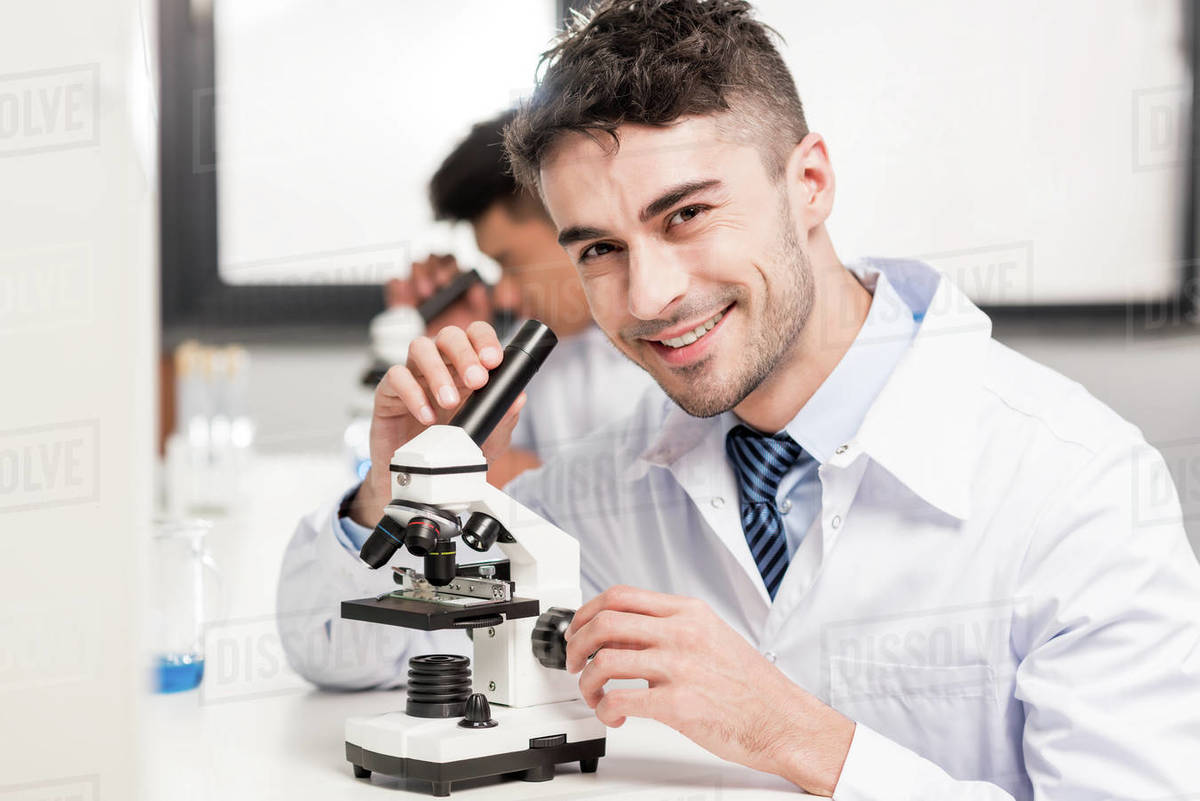 Young handsome doctor working with microscope in laboratory and smiling ...
