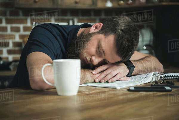 Portrait of tired man sleeping on table with newspaper and coffee cup ...