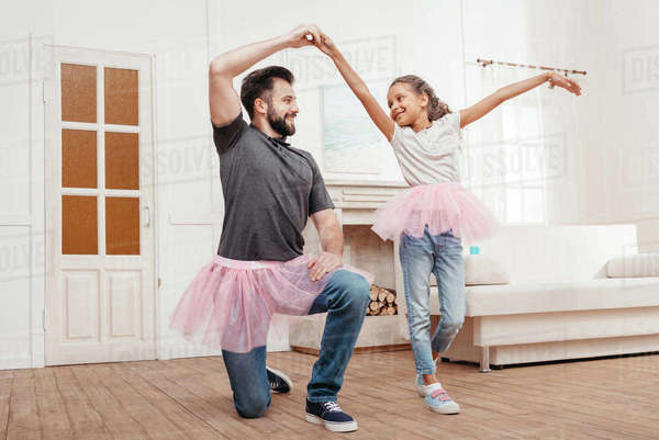 Multicultural father and daughter in pink tutu tulle skirts dancing at ...
