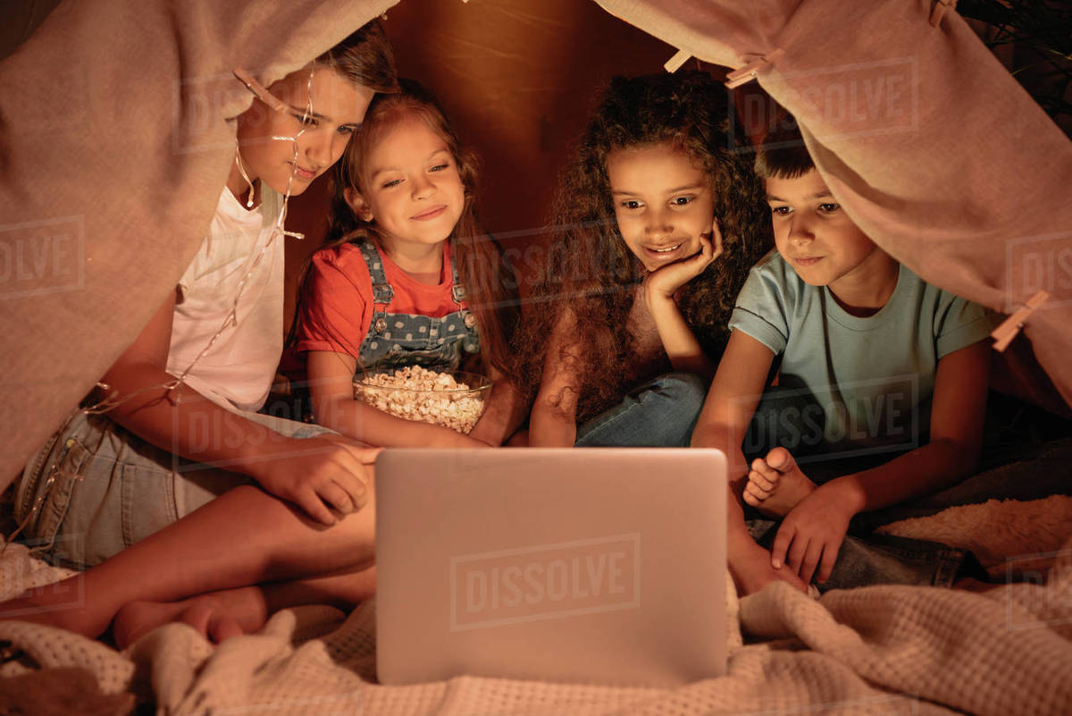 Little multiethnic kids sitting tent and watching film together ...