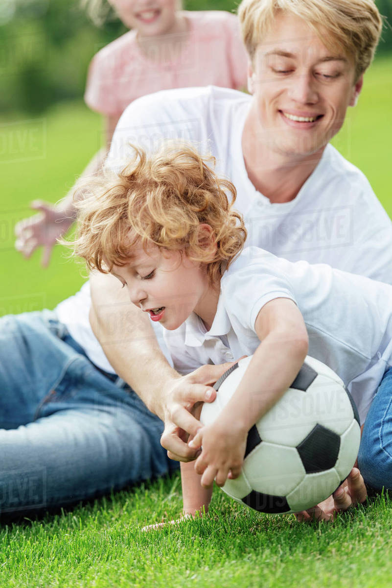 Happy father and son playing with soccer ball on green grass at park ...