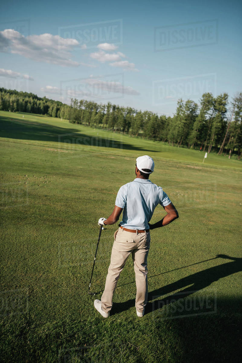 Back view of golfer holding club and looking away at green lawn ...