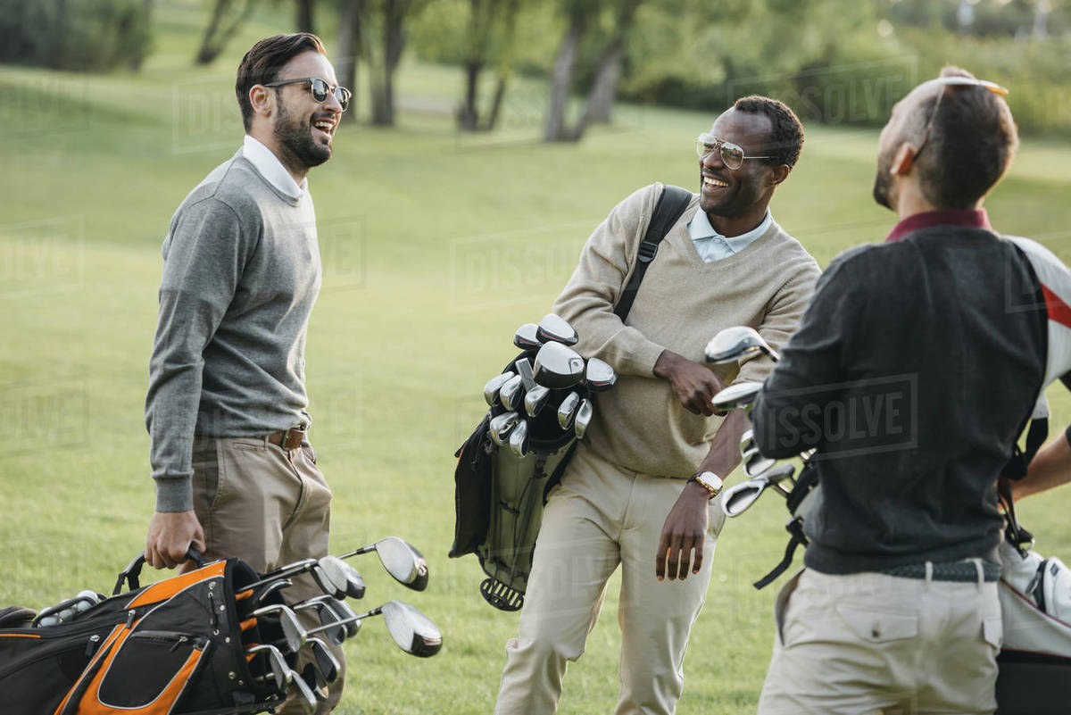 Multiethnic golf players with golf clubs having fun on golf course ...