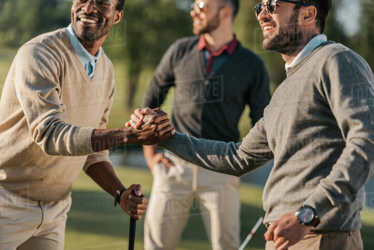 Happy multicultural friends shaking hands while playing golf on golf ...