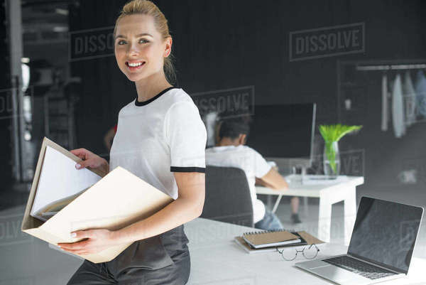 Beautiful young businesswoman holding folder with documents and smiling ...
