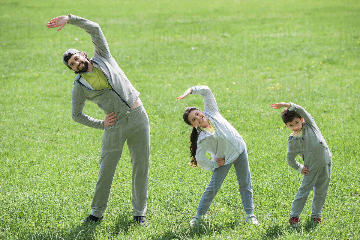 Father with daughter and son doing physical exercise on grass - Royalty ...