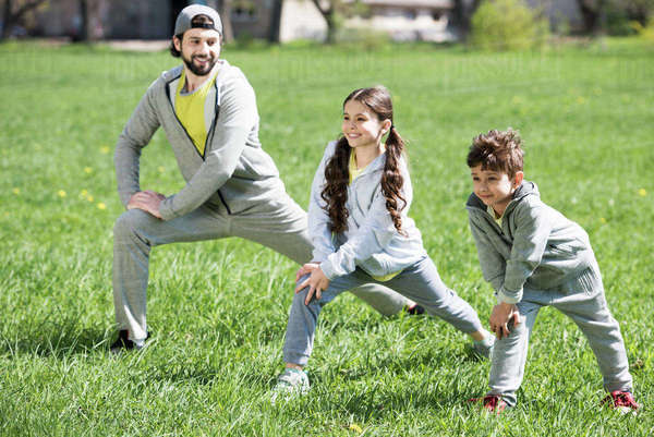 Father with daughter and son doing physical exercise on grassy meadow ...