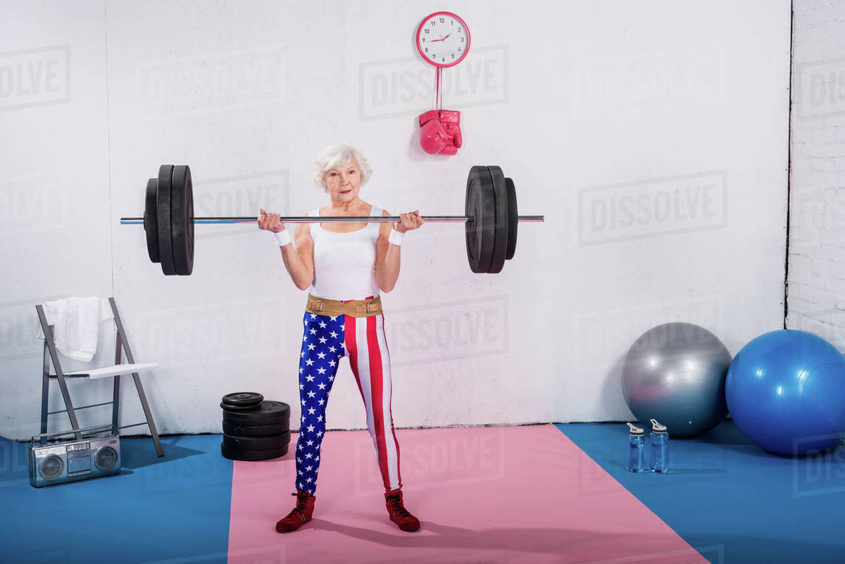 Sporty senior lady lifting barbell and looking at camera - Stock Photo ...